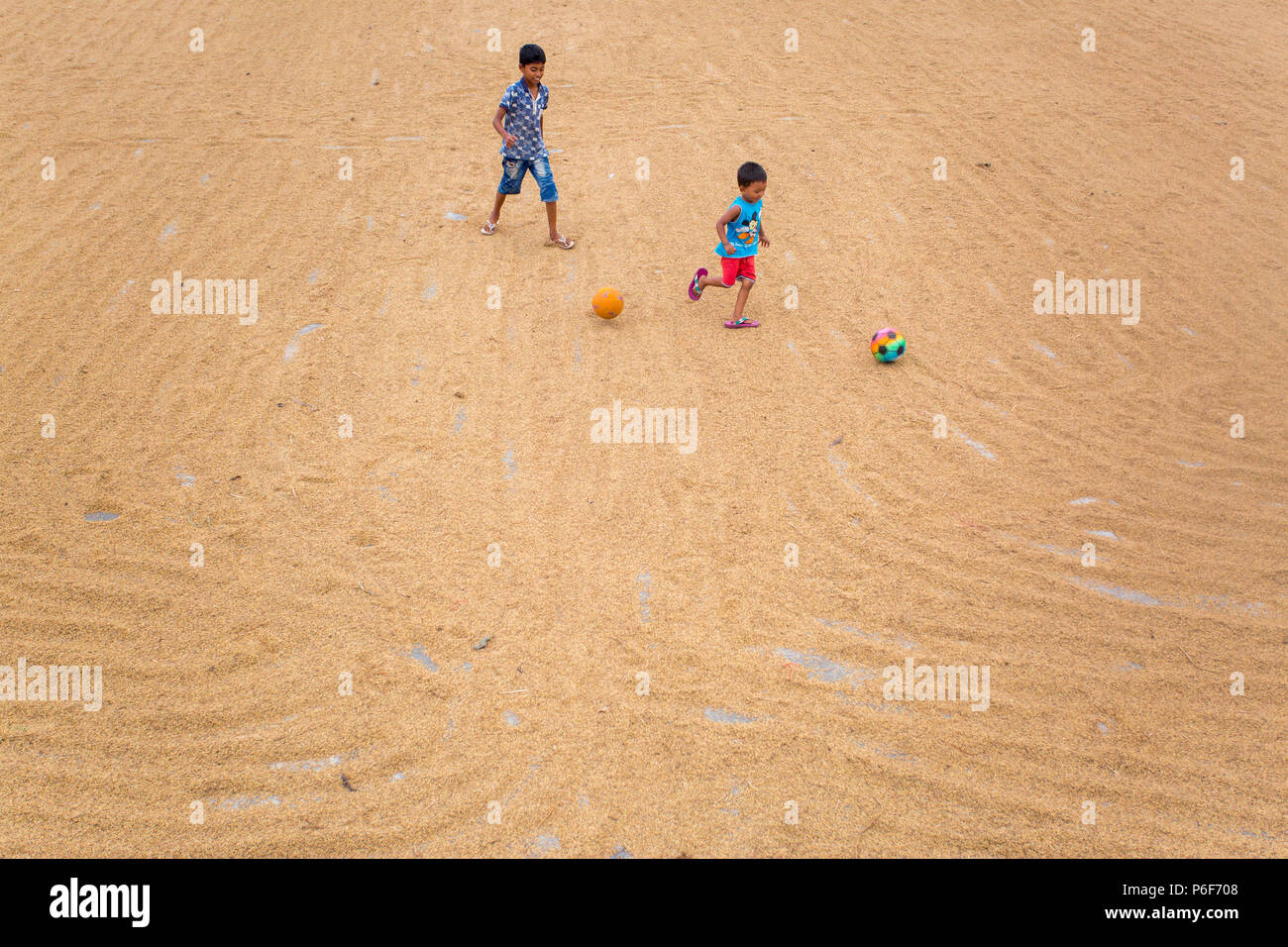 Some of the children are playing football on dry paddy in the sun at ...
