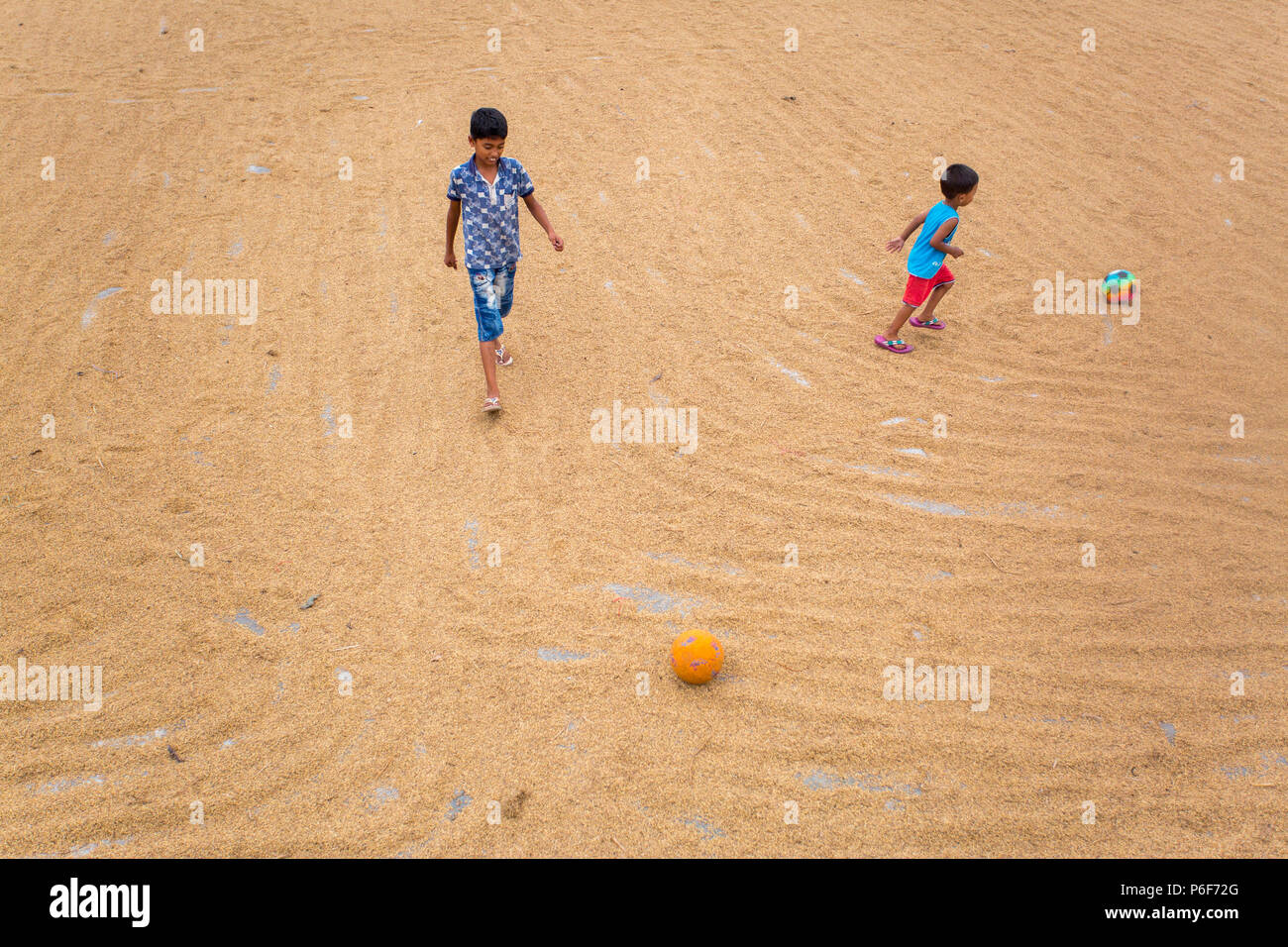 Some of the children are playing football on dry paddy in the sun at ...