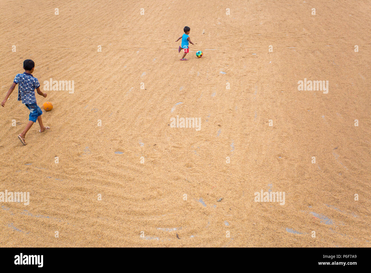 Some of the children are playing football on dry paddy in the sun at ...