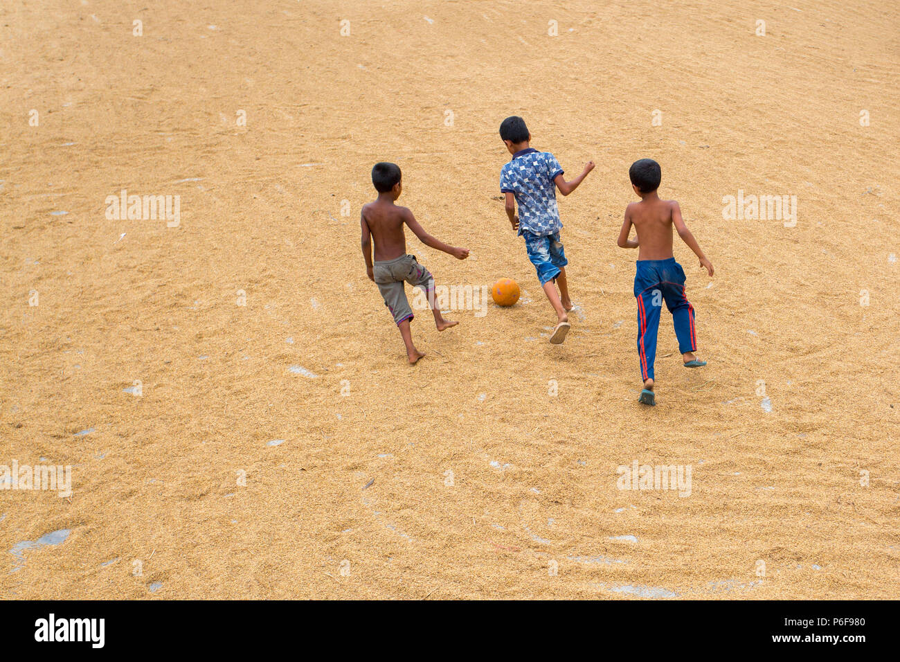 Some of the children are playing football on dry paddy in the sun at ...