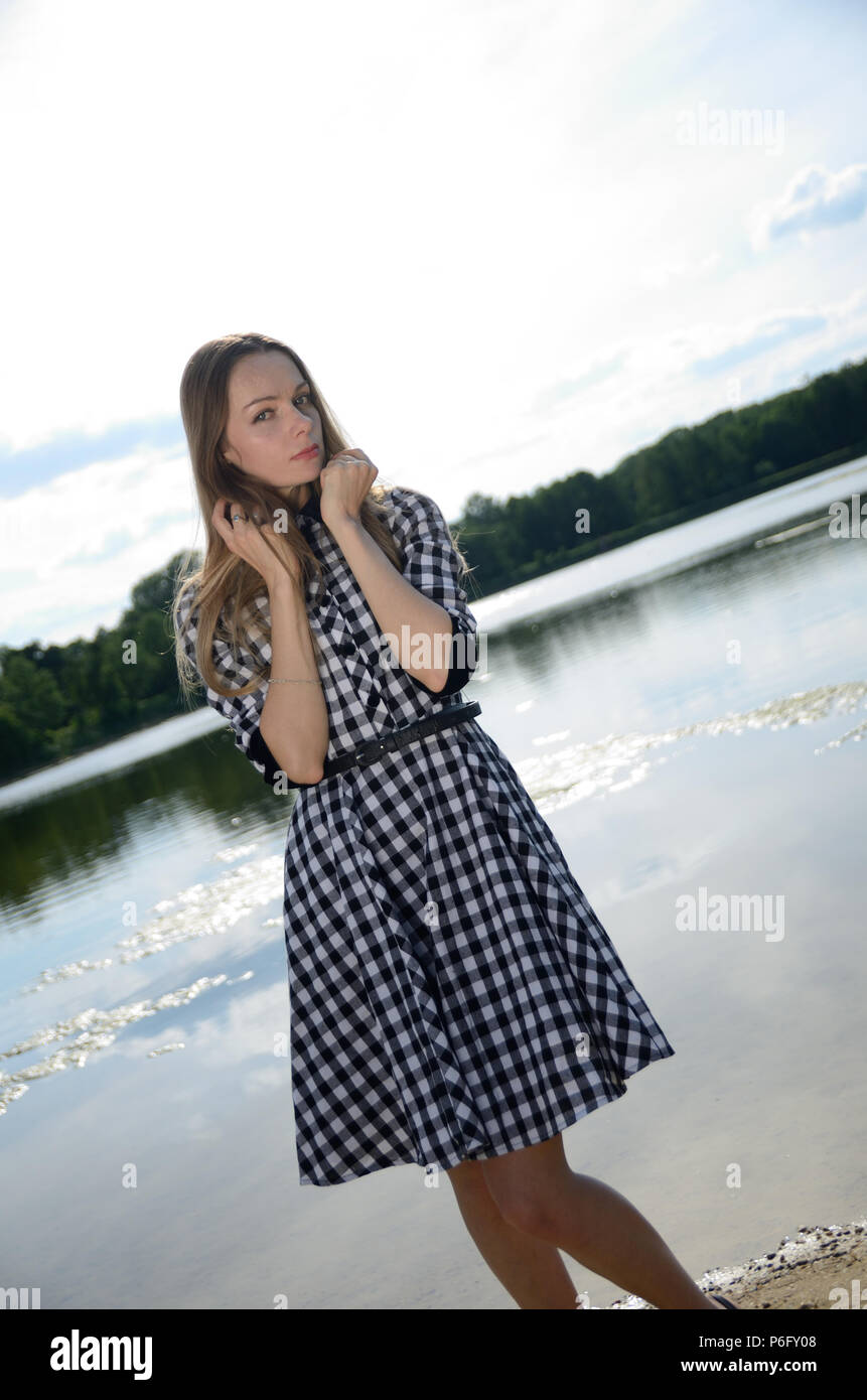 Petite woman at lake. Female model with black-white dress posing near ...