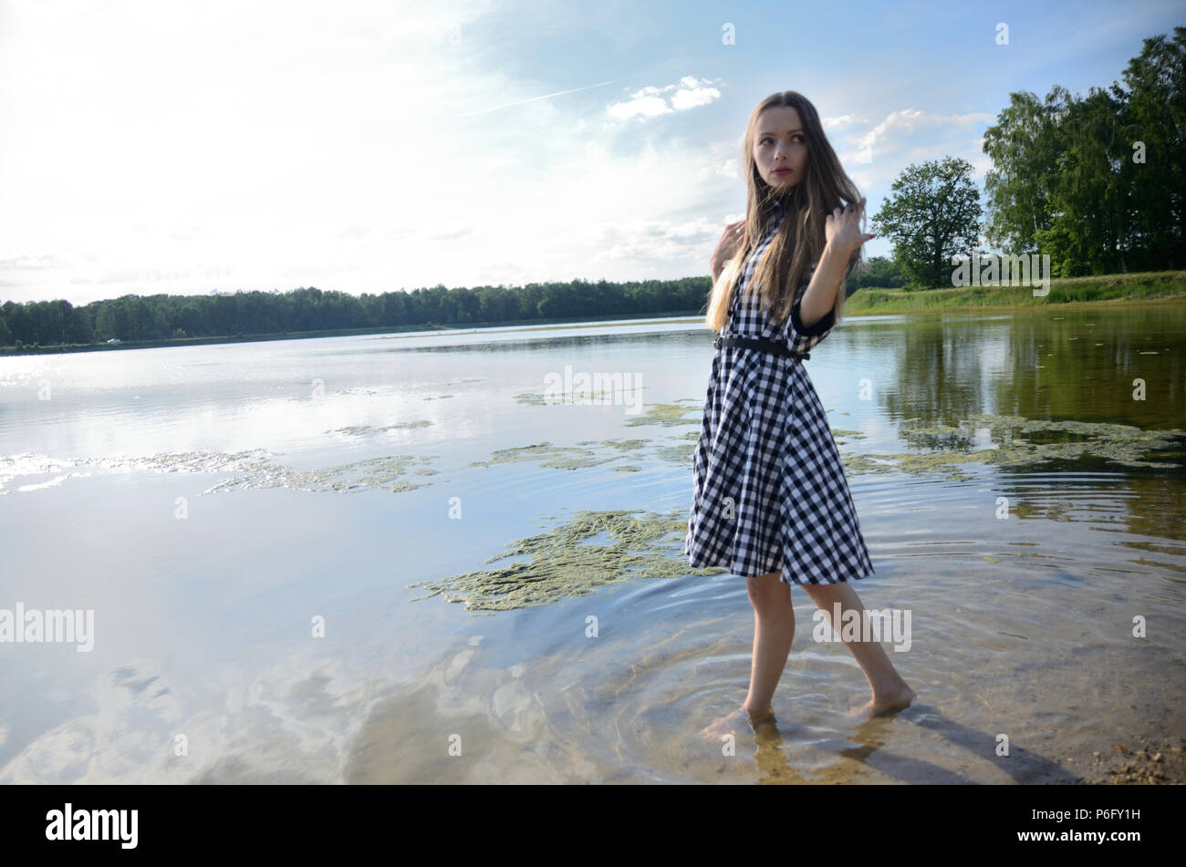 Petite woman at lake. Female model with black-white dress posing near ...