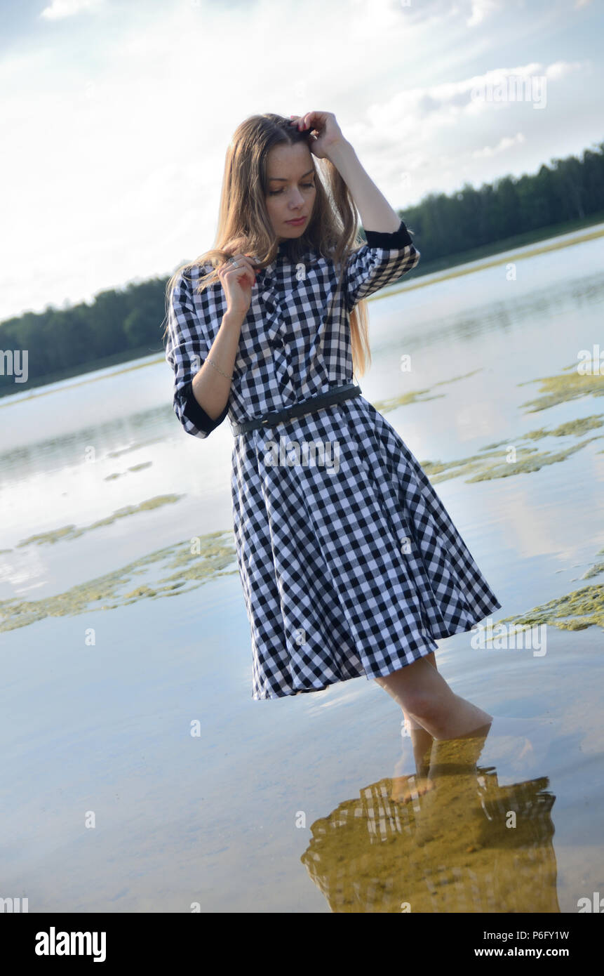 Petite woman at lake. Female model with black-white dress posing near ...