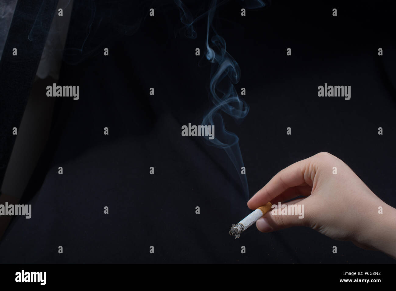 Hand is holding smoking cigarette with smoke around Stock Photo - Alamy