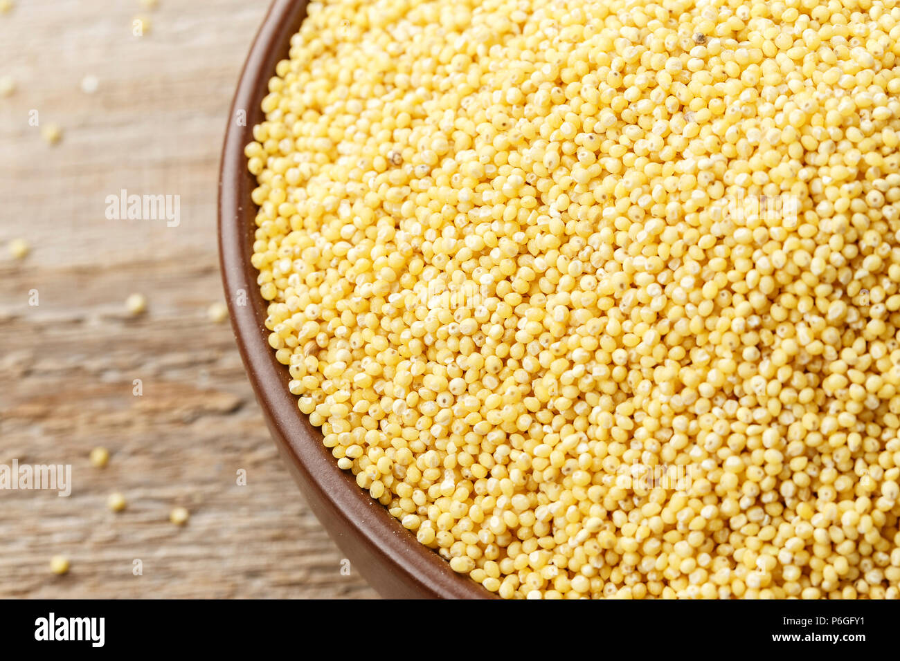 raw millet grains in a clay plate on a wooden background, top view ...