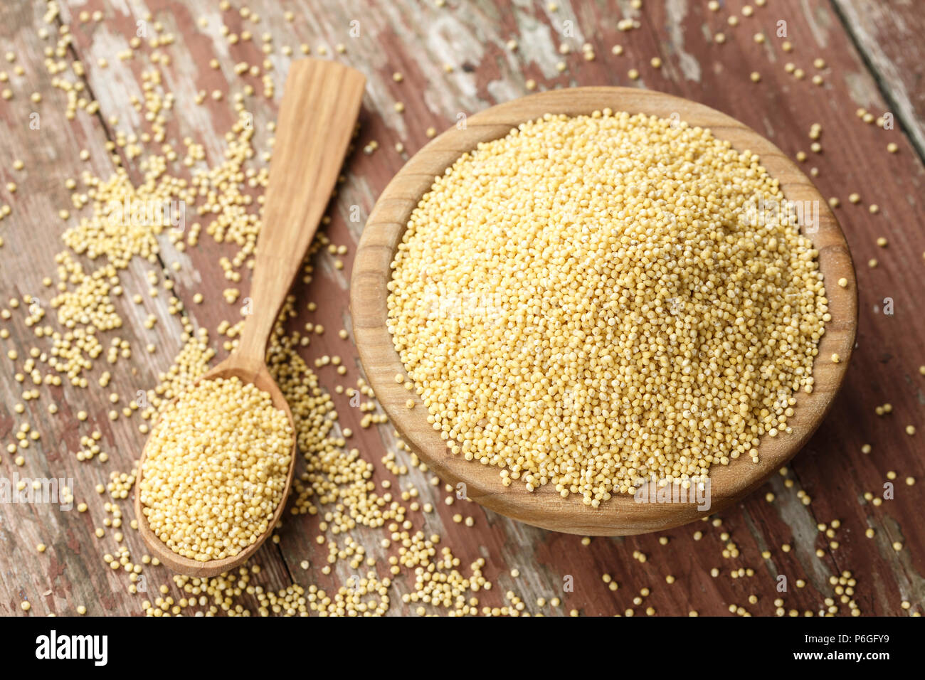raw millet cereal in a wooden plate on a wooden background, next to it ...