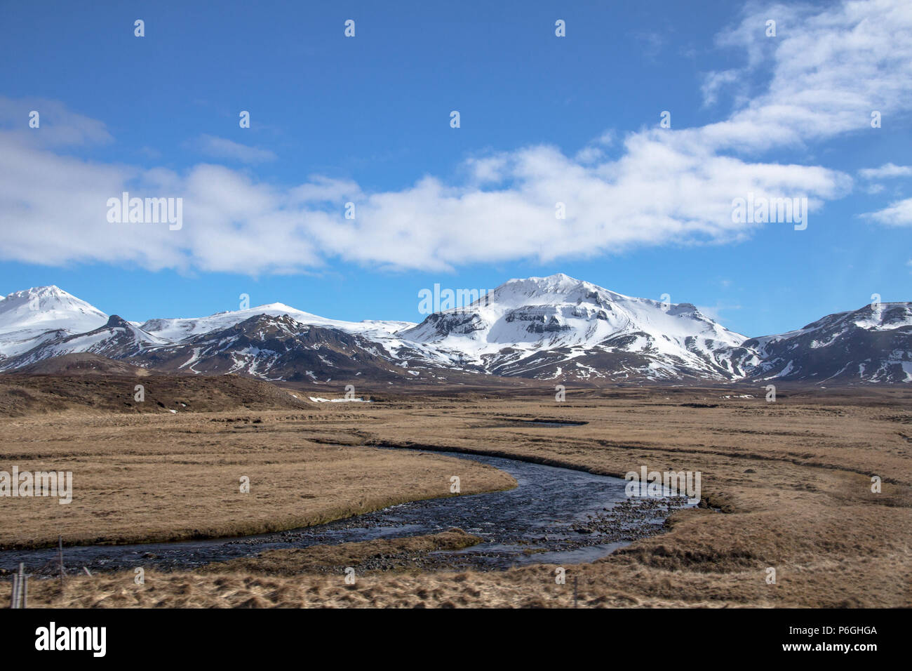 A shallow river from snow-covered mountains, winds over a grassy plain ...