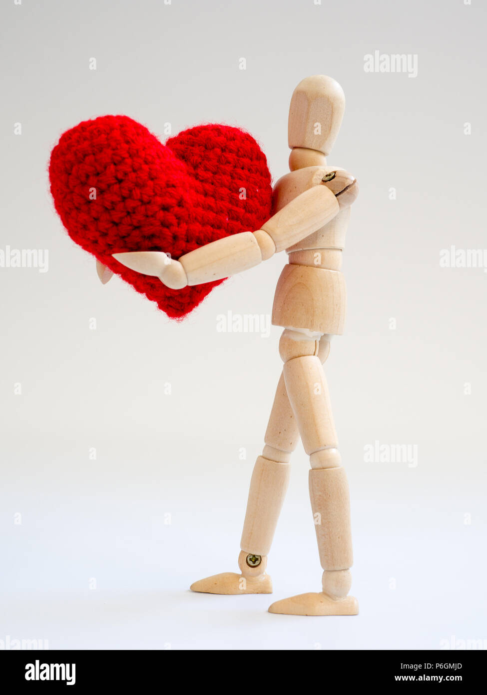 Wooden puppet standing and holding a red heart on the white screen ...