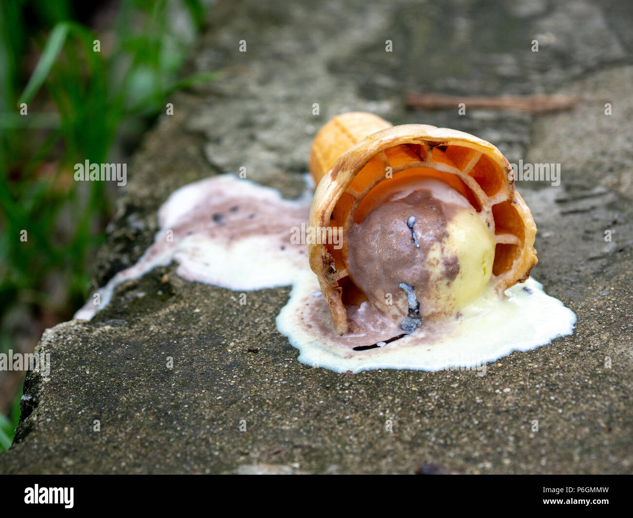 A rainbow ice cream cone dropped on the concrete floor and melting on ...