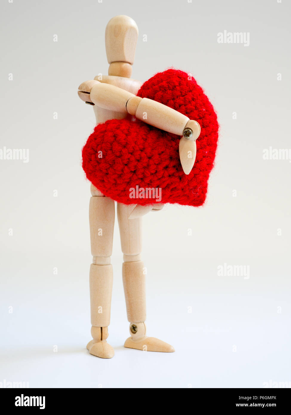 Wooden puppet standing and holding a red heart on the white screen ...