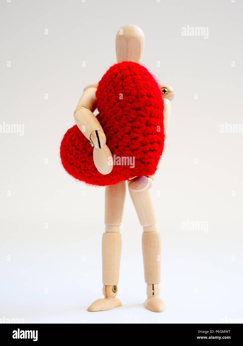 Wooden puppet standing and holding a red heart on the white screen ...