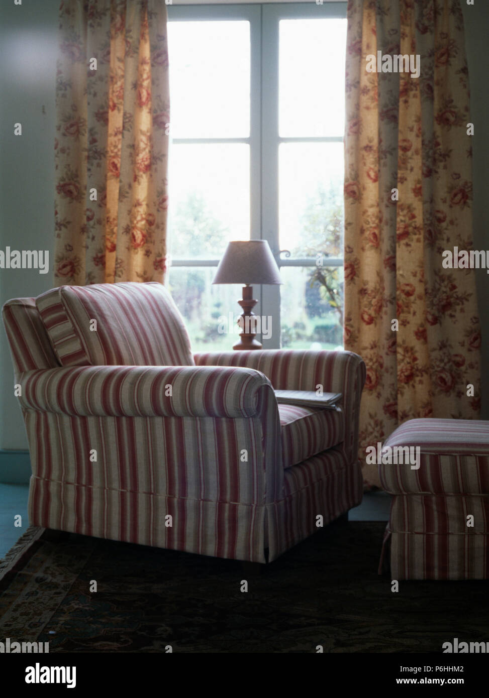 Striped armchair and stool in front of window with floral curtains in ...