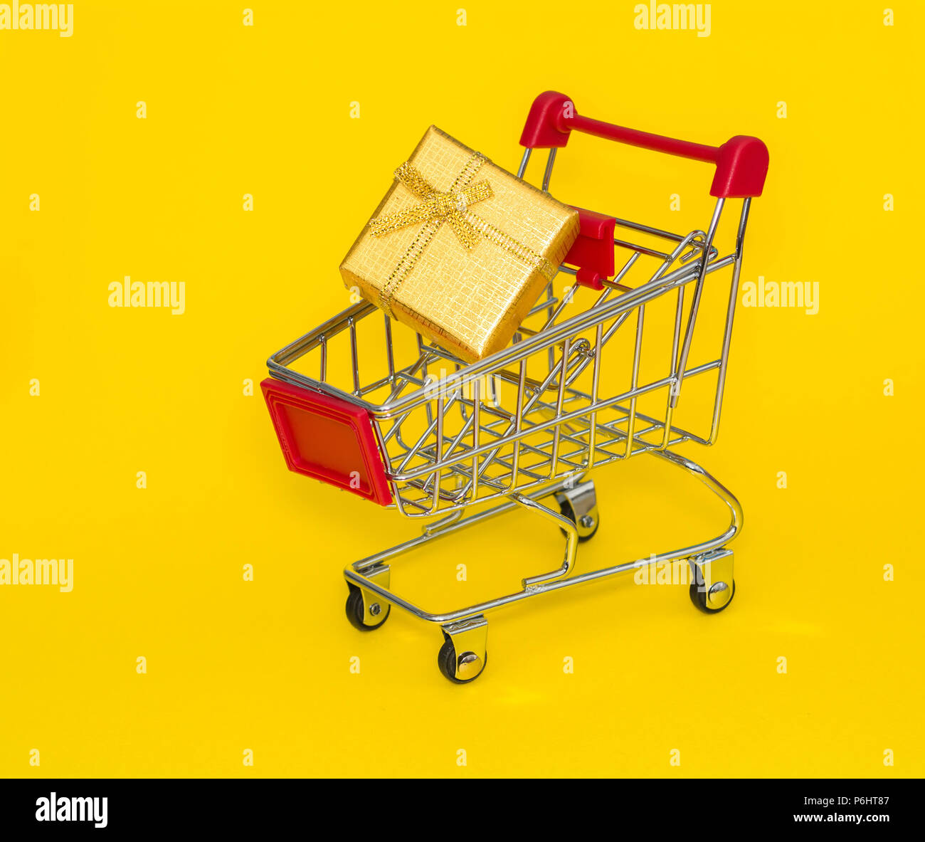 Shopping trolley with gold gift on a yellow background Stock Photo - Alamy