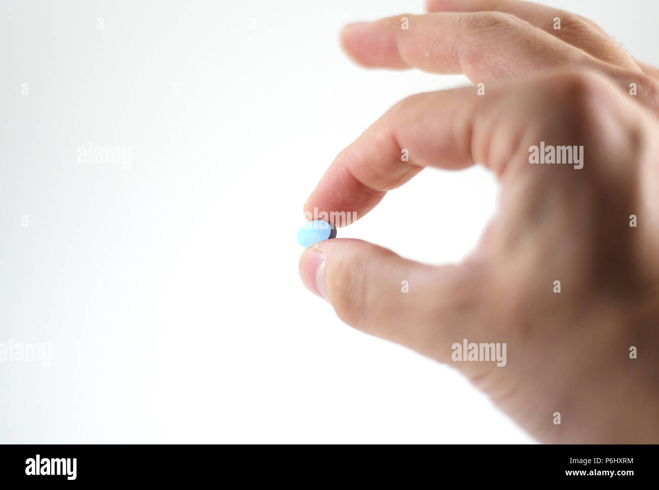 Male hand holding blue pill between fingers - isolated Stock Photo - Alamy