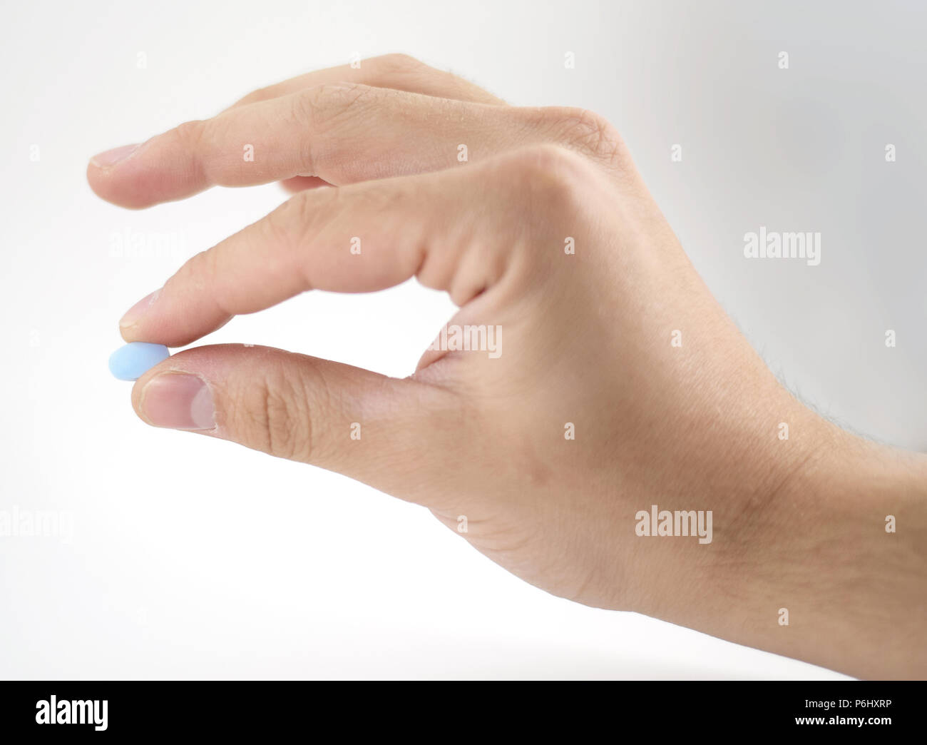 Male hand holding blue pill between fingers - isolated Stock Photo - Alamy