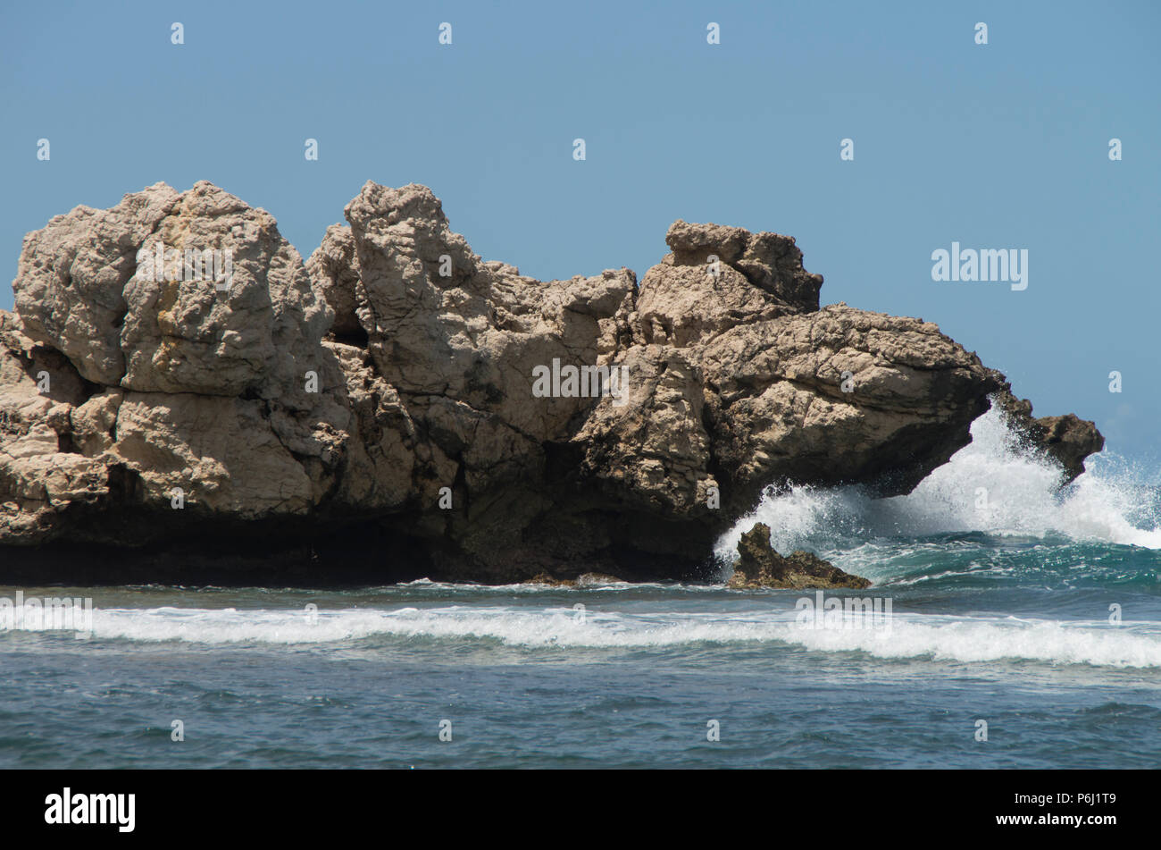 Waves crash against a large rock outcrooping along the shoreline in ...