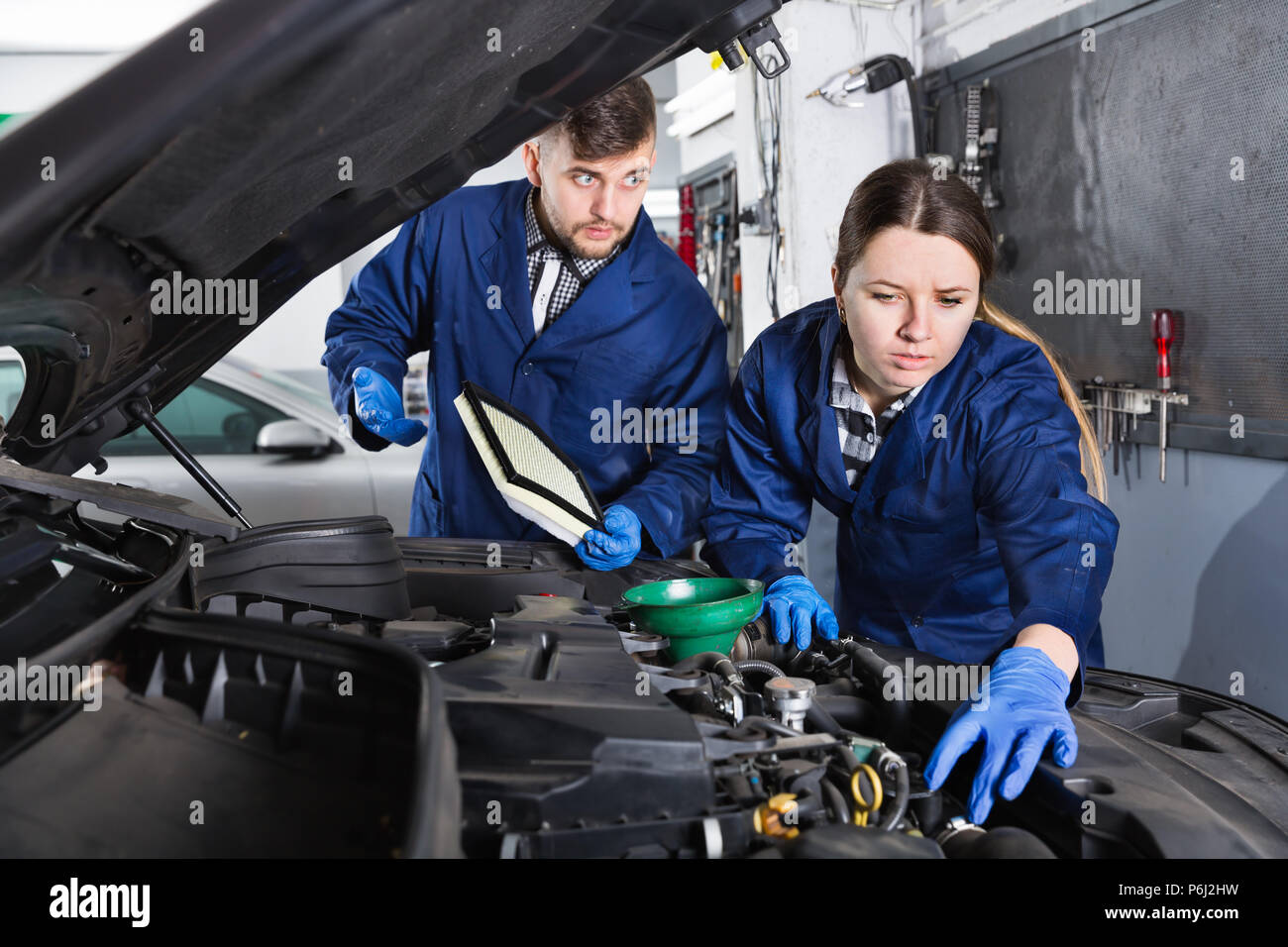 Young female master with foreman are replacing the oil in the car in ...