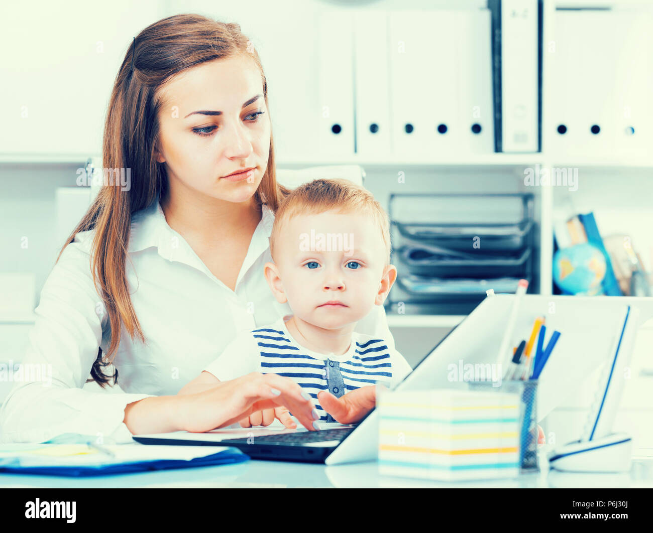 Female with child is working behind laptop in office Stock Photo - Alamy