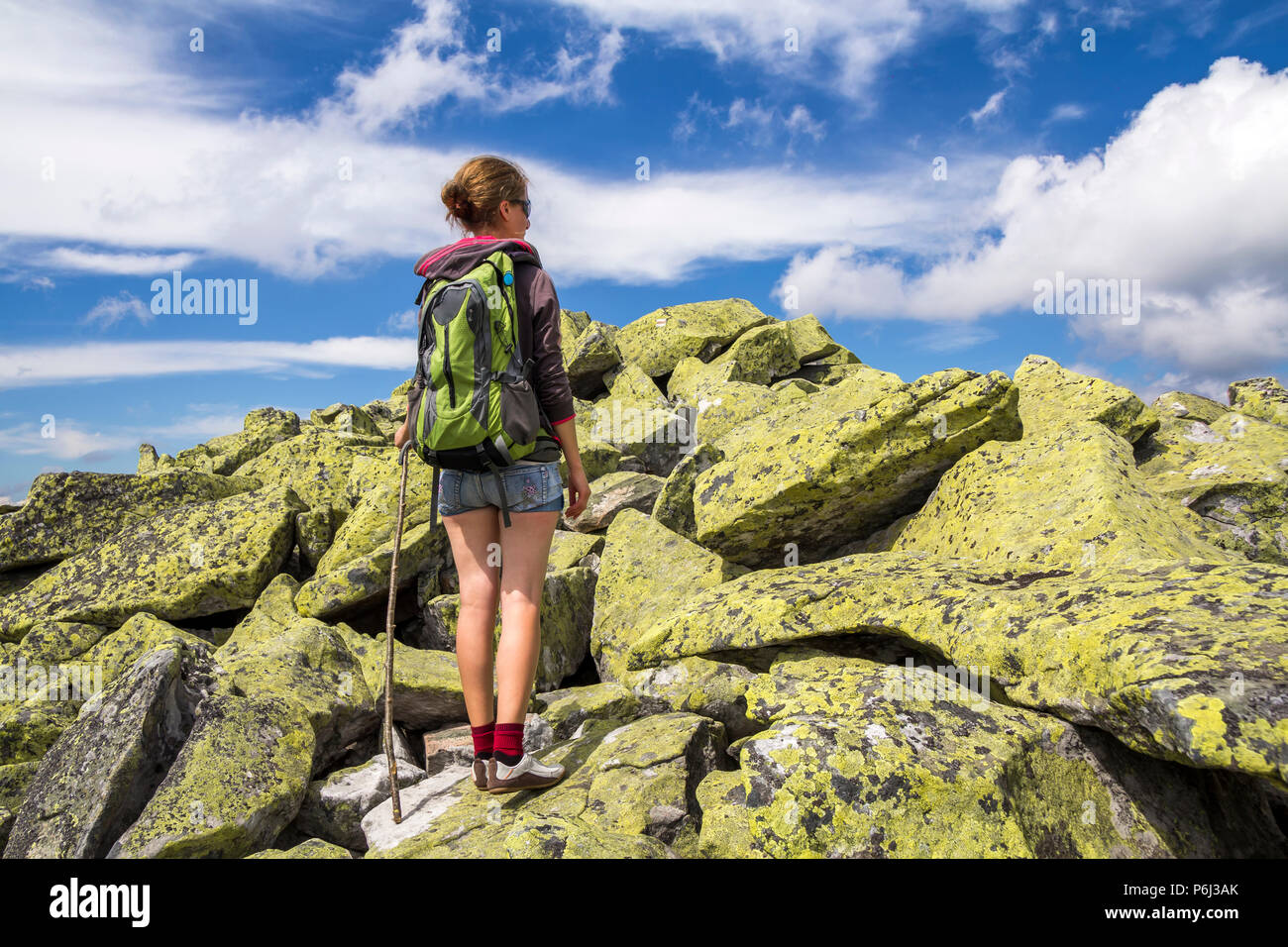 Slim athletic blond tourist hiker girl with stick and backpack climbing ...