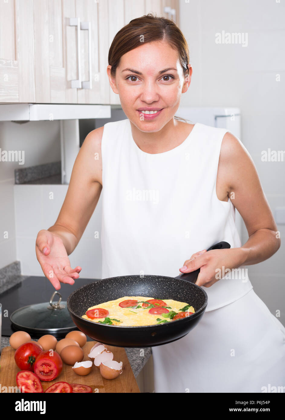 glad young woman holding frying pan with omelet at kitchen unit indoors ...