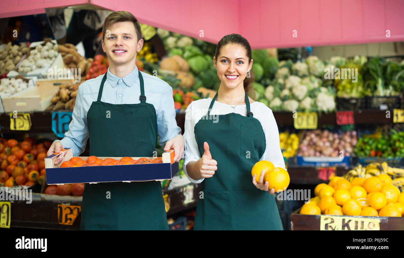 Positive supermarket workers offering fruits in vegetables section ...