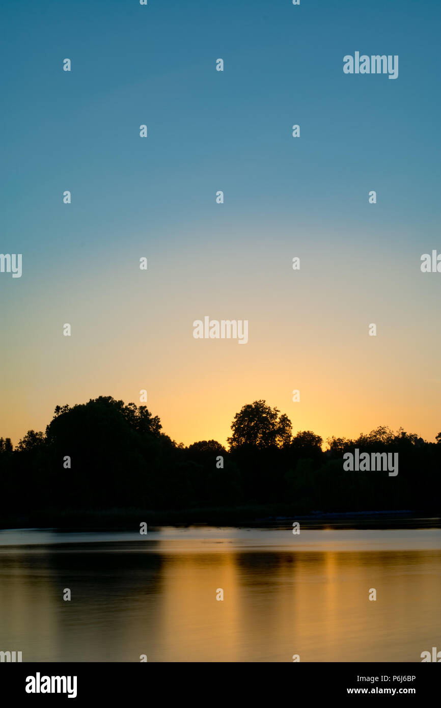 Portrait long exposure sunset over a lake with silhouettes of trees in ...