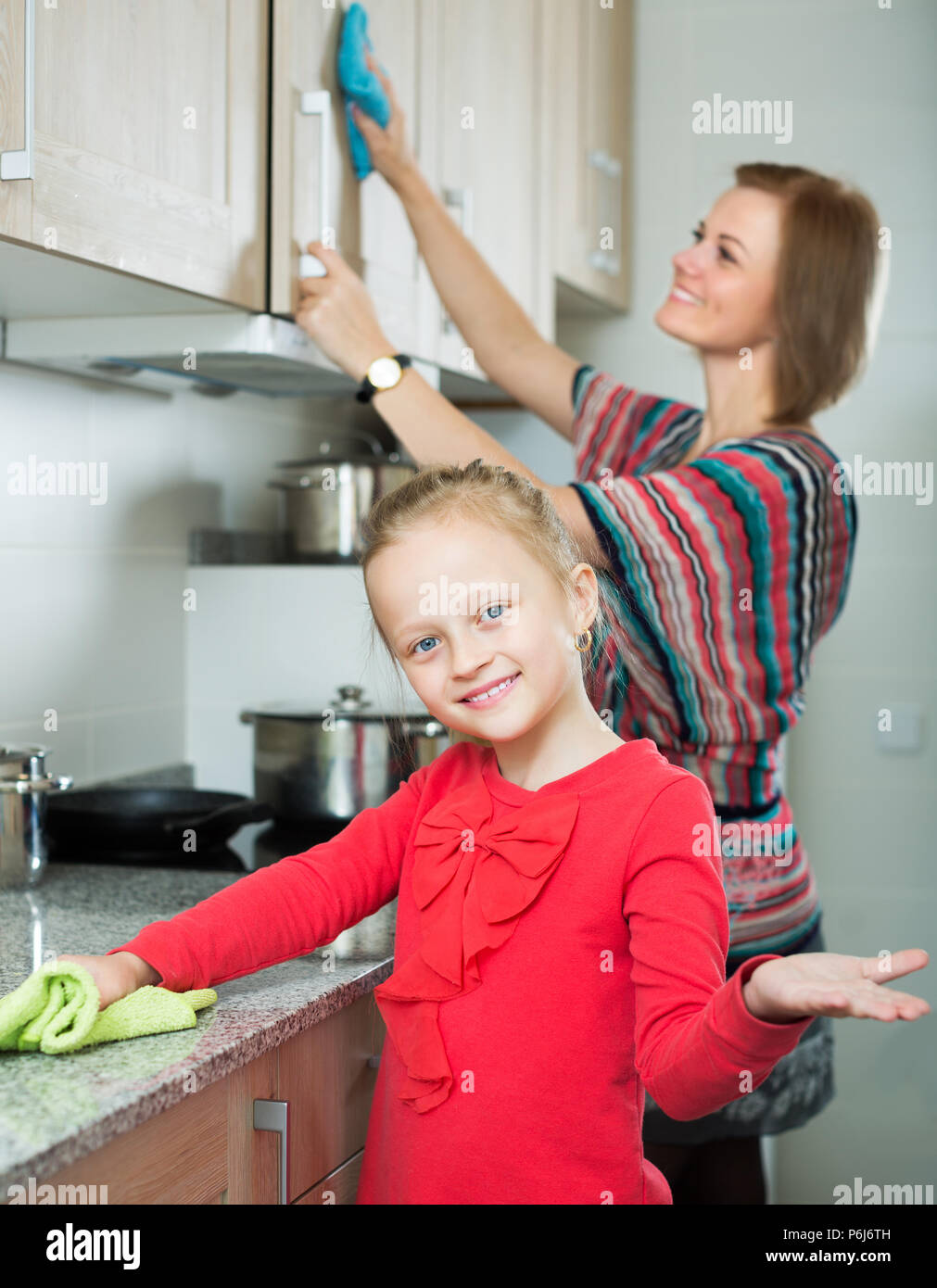 Blonde smiling girl helping mother dusting furniture indoor Stock Photo ...