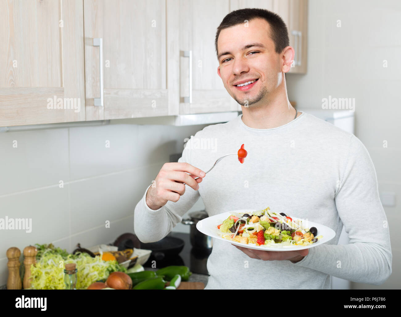 Portrait of joyful young guy eating vegetable salad in kitchen Stock ...