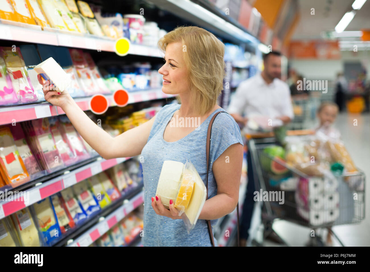 Portrait of happy woman holding assortment of cheese in grocery shop ...