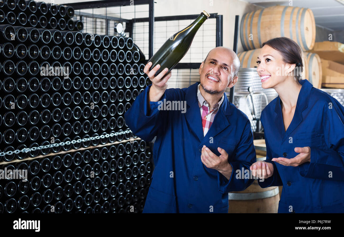 cheerful man and women coworkers looking at bubbly wine in bottle ...
