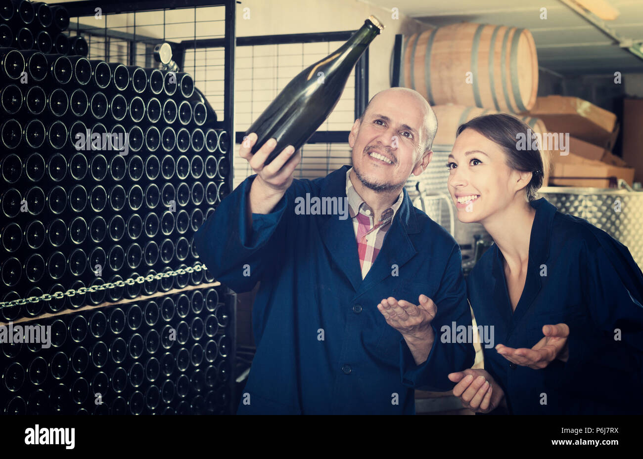 Cheerful winery workers holding bottle of sparkling wine in aging ...