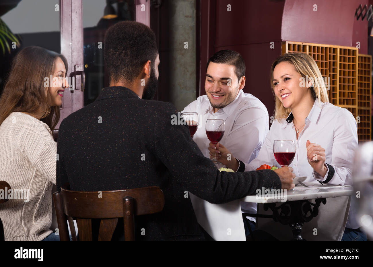 Group of cheerful smiling young friends eating at restaurant table and ...