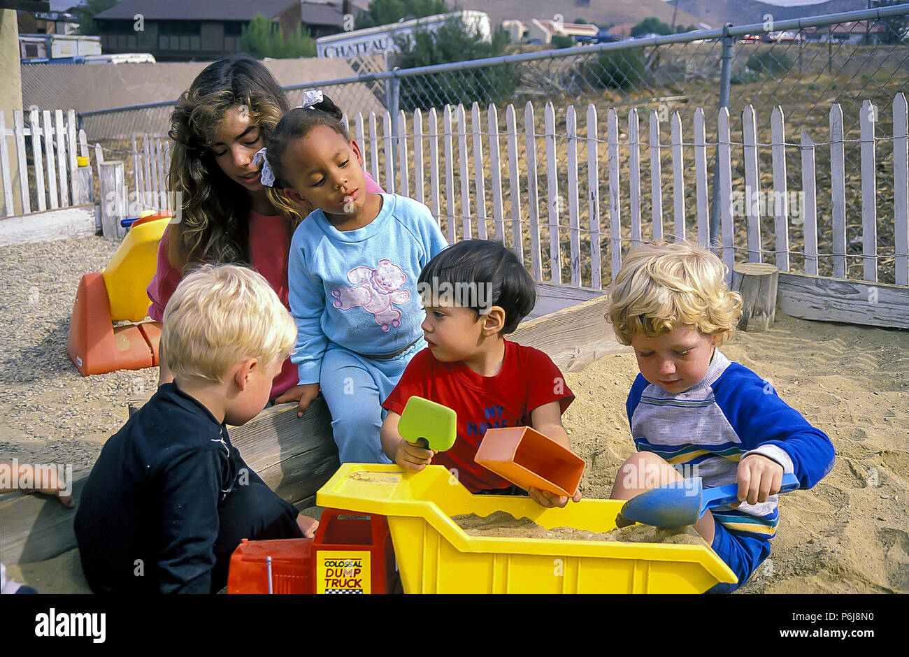 Children playing in sand box as young woman supervises
