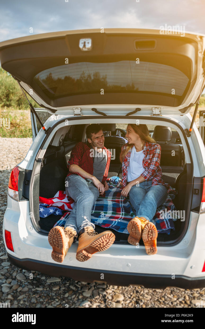 Happy traveler couple sitting in car open trunk and communicate at ...