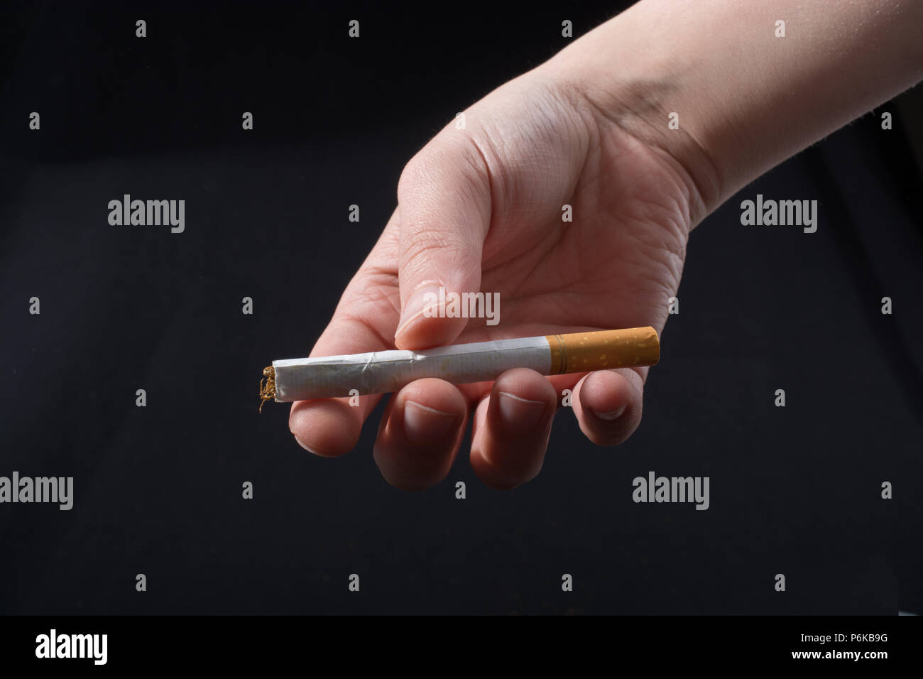 Hand is giving out cigarette on a black background Stock Photo - Alamy