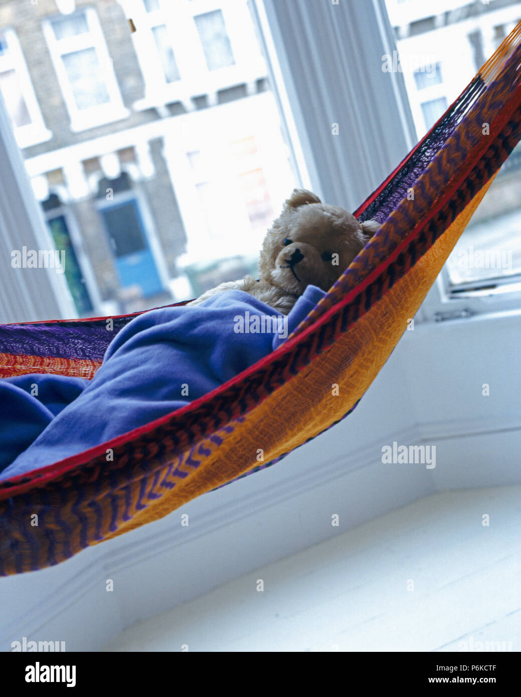Close-up of teddy bear wrapped in blue blanket in colourful hammock ...