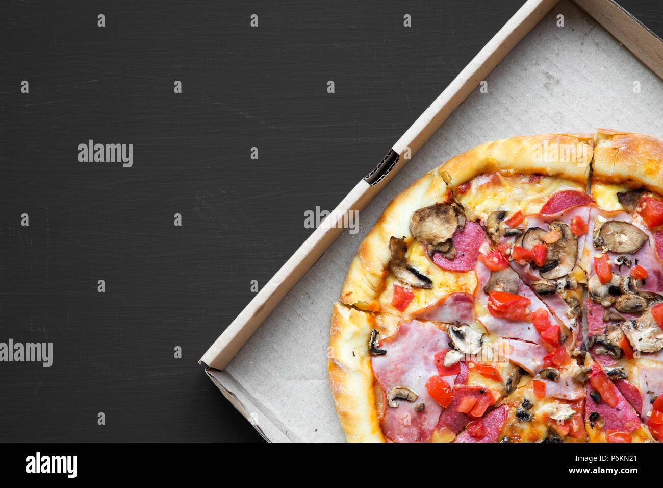 Freshly baked pizza in a cardboard box on black table, top view. Copy ...
