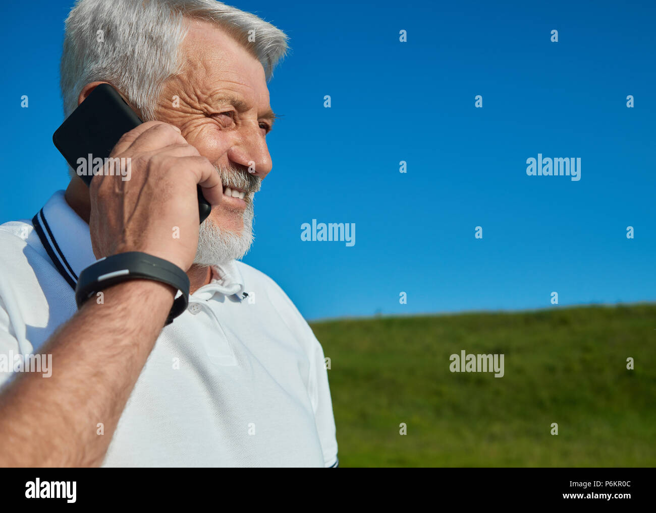 Old man talking on cell phone in green field. Looking positive, smiling ...