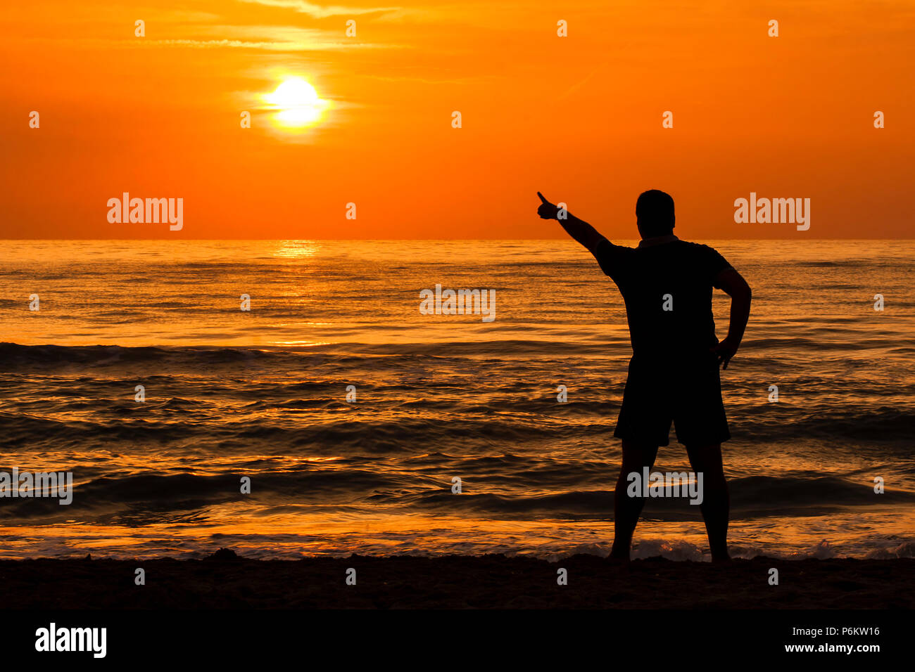 Silhouette of young man pointing out the sun at dawn at sea Stock Photo ...