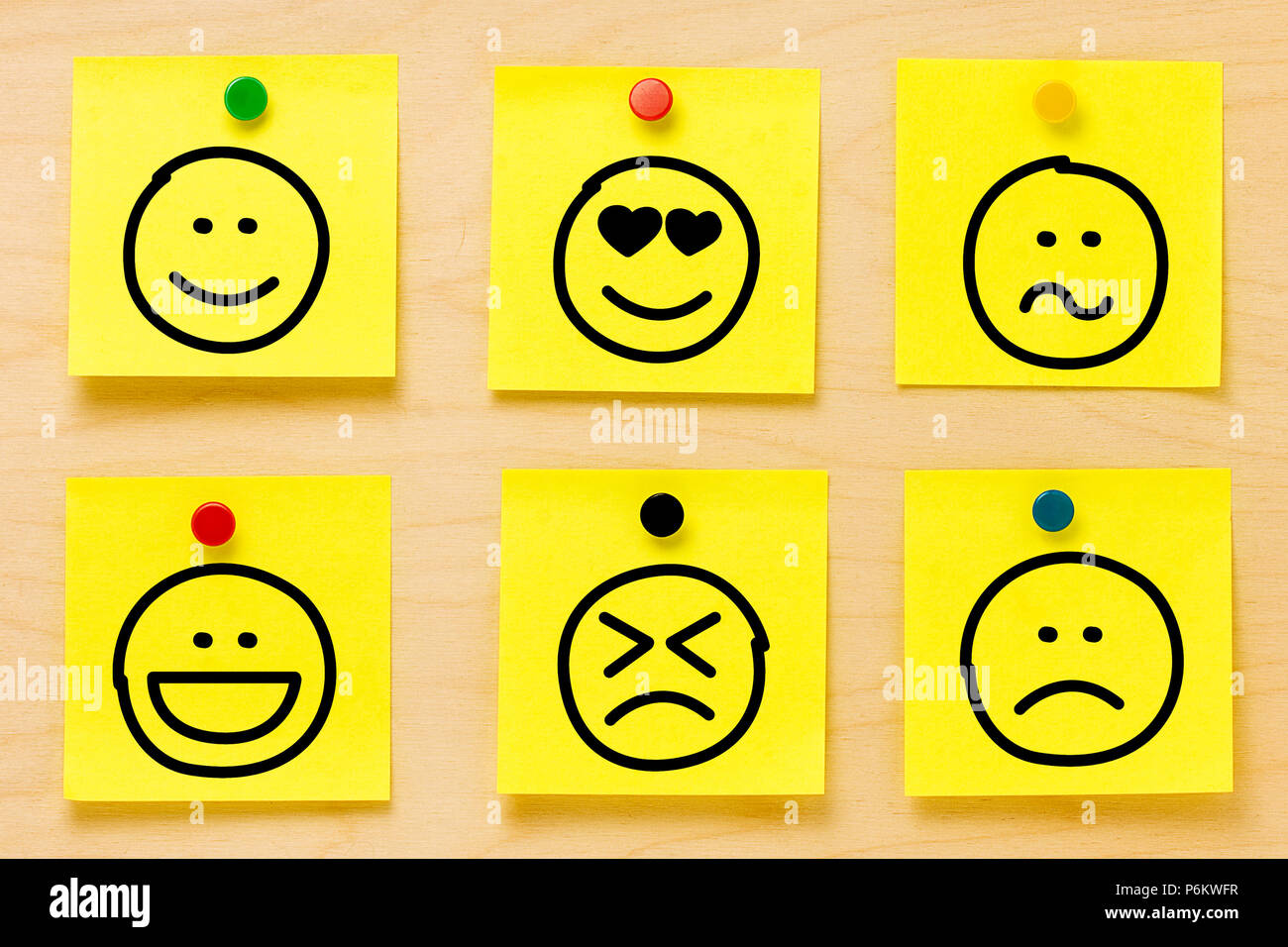 Hand drawing emoticons on six yellow postit notes affixed by colored ...