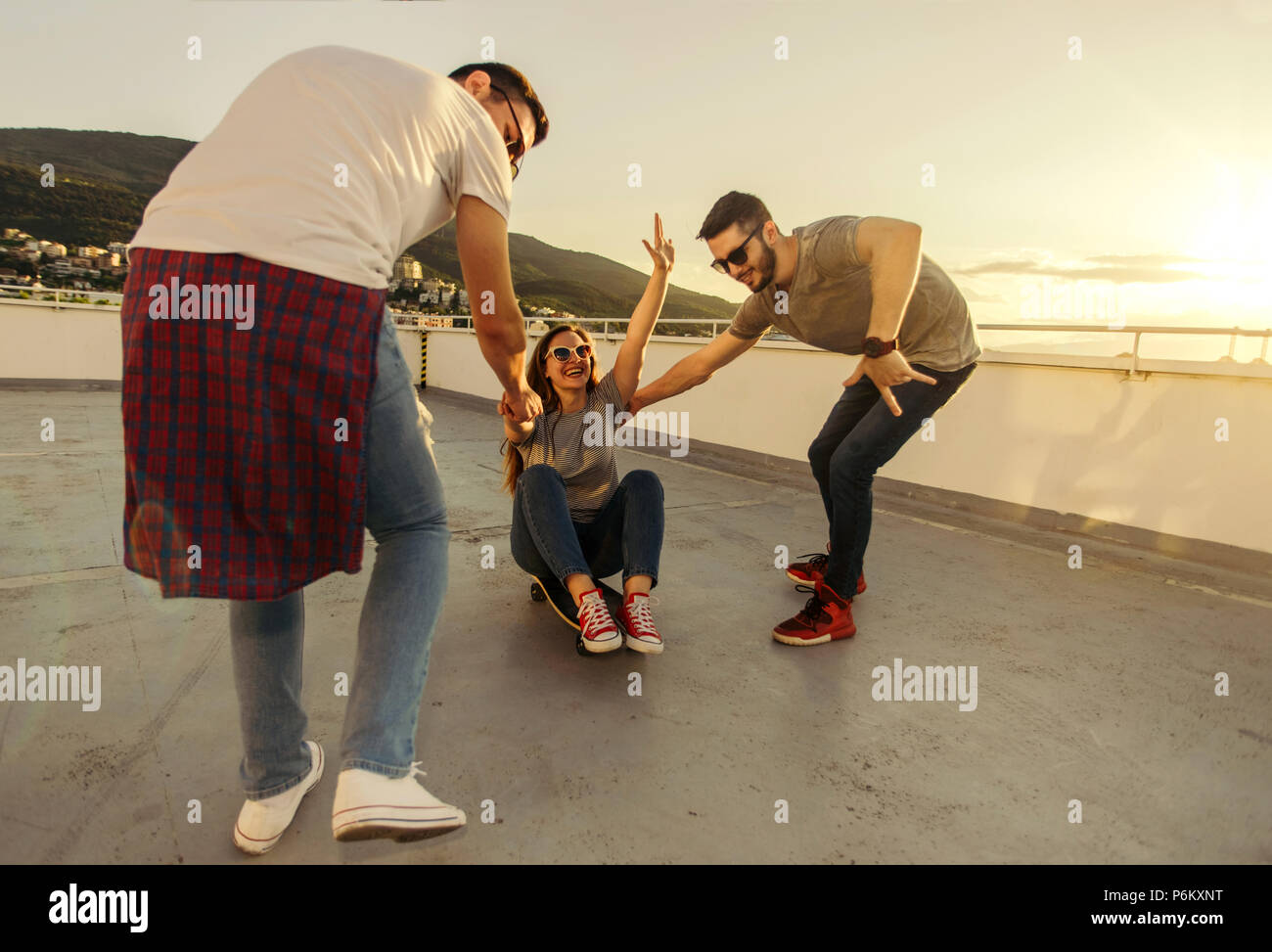 Two Caucasian friends pushing his friend on skateboard on the rooftop ...