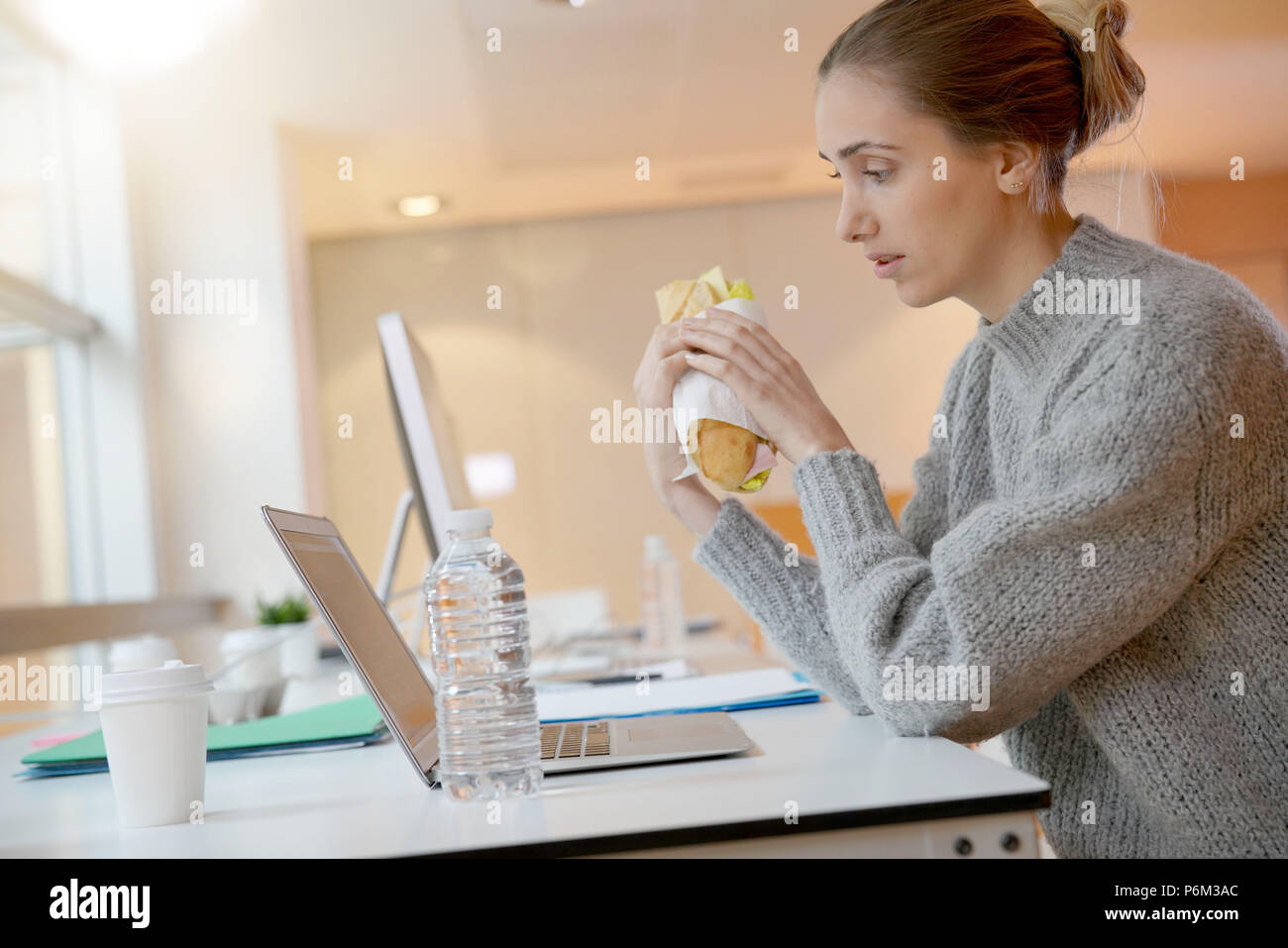 Young woman student eating sandwich in front of laptop computer Stock ...