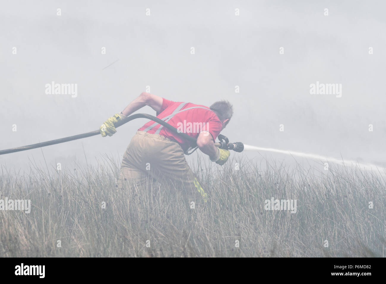 Lancashire, UK. 1 July 2018 - A male firefighter struggles to pull a ...