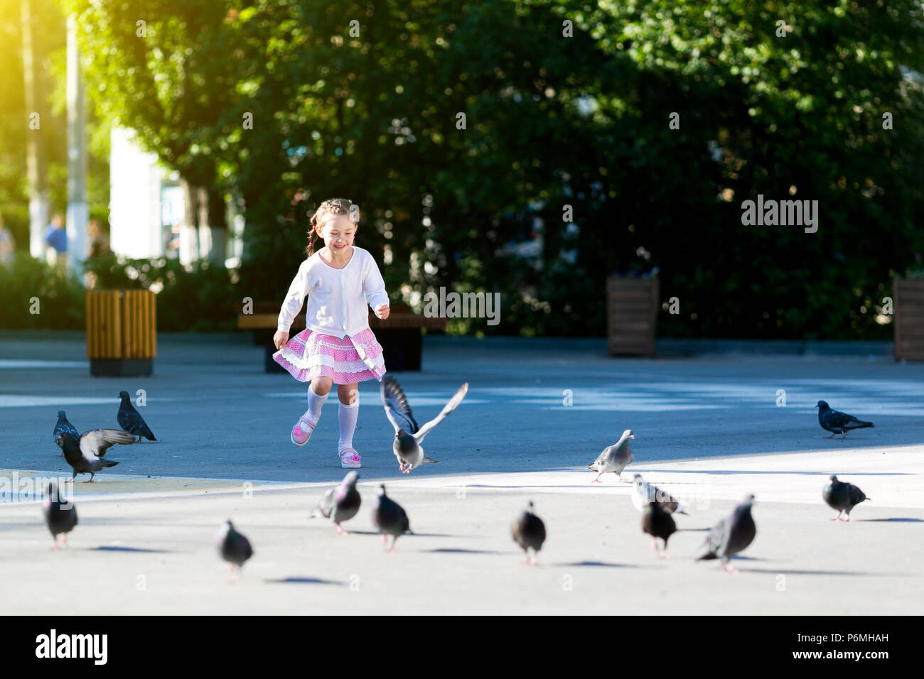 A little girl in a pink dress is catching the birds in the town square ...