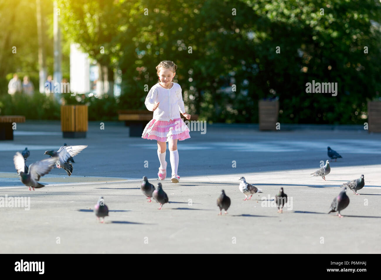 A little girl in a pink dress is catching the birds in the town square ...