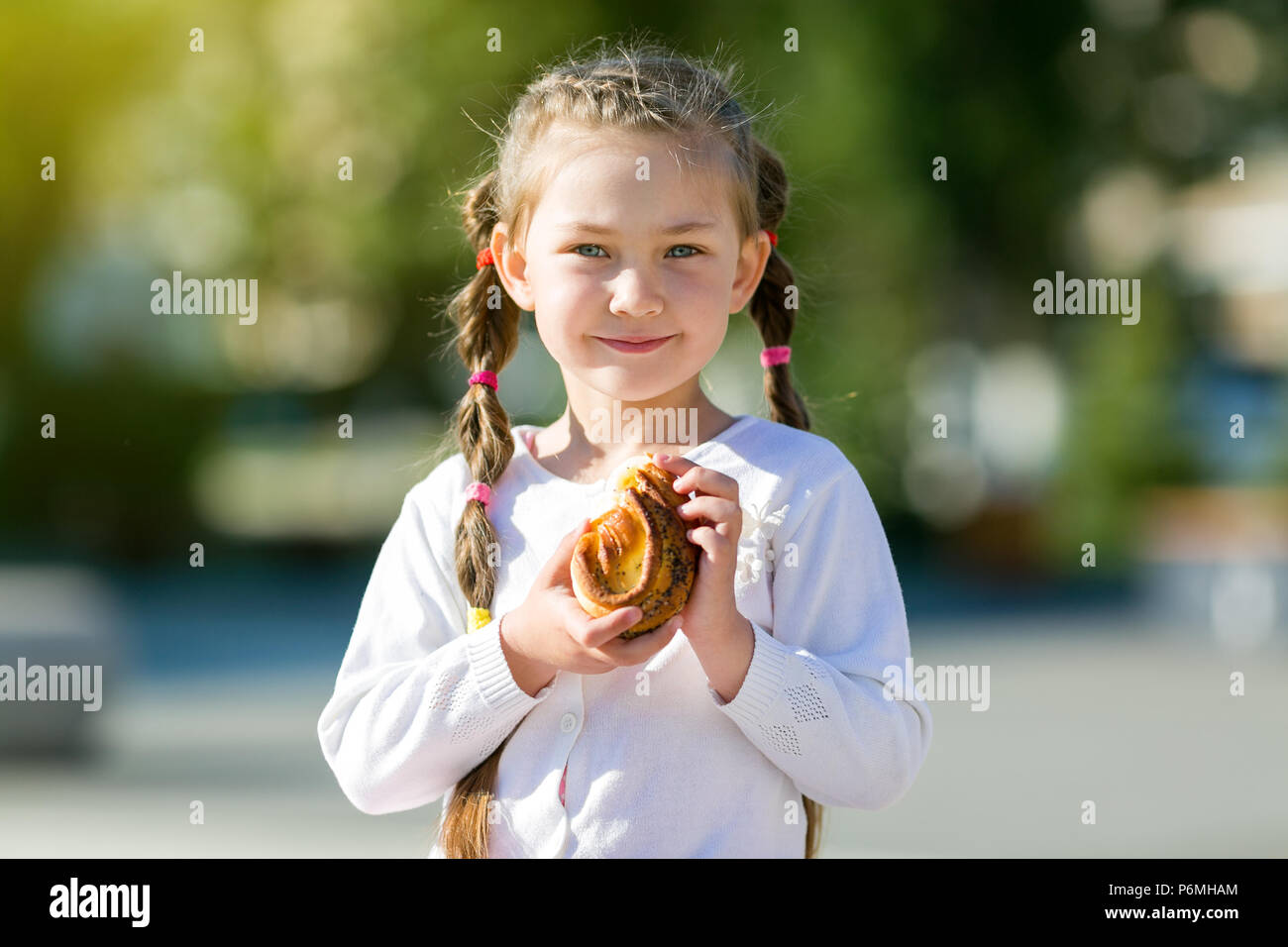 A beautiful girl bites a big sweet bun Stock Photo - Alamy