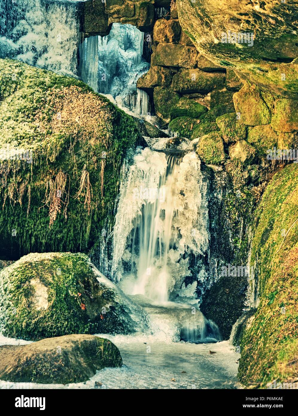Winter frozen waterfall. Small pond and snowy boulders bellow cascade ...