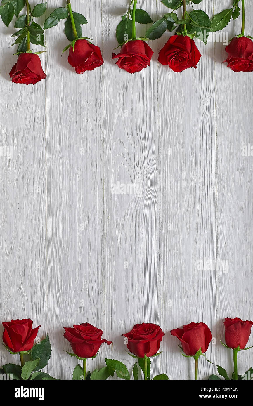 Frame of red roses on white wooden background. With space for text ...