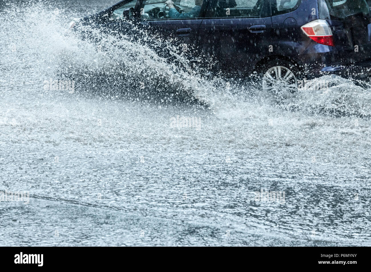 car moving with high speed through water puddle on flooded city road ...