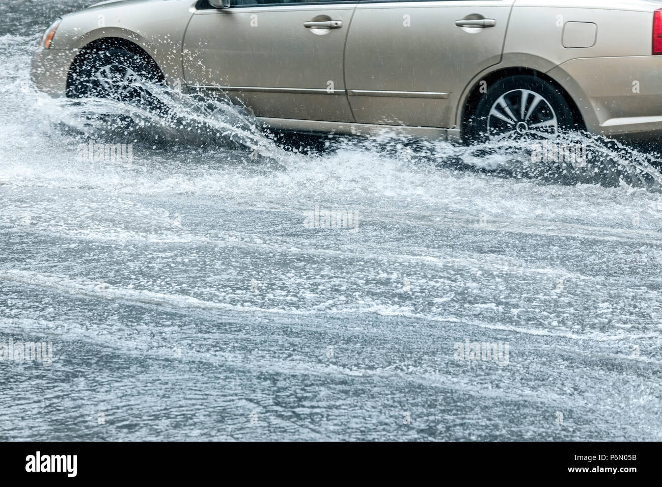 flooded city road with car moving and splashing rain water from wheels ...